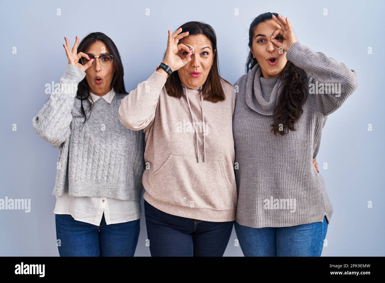 Mother and two daughters standing over blue background doing ok gesture ...