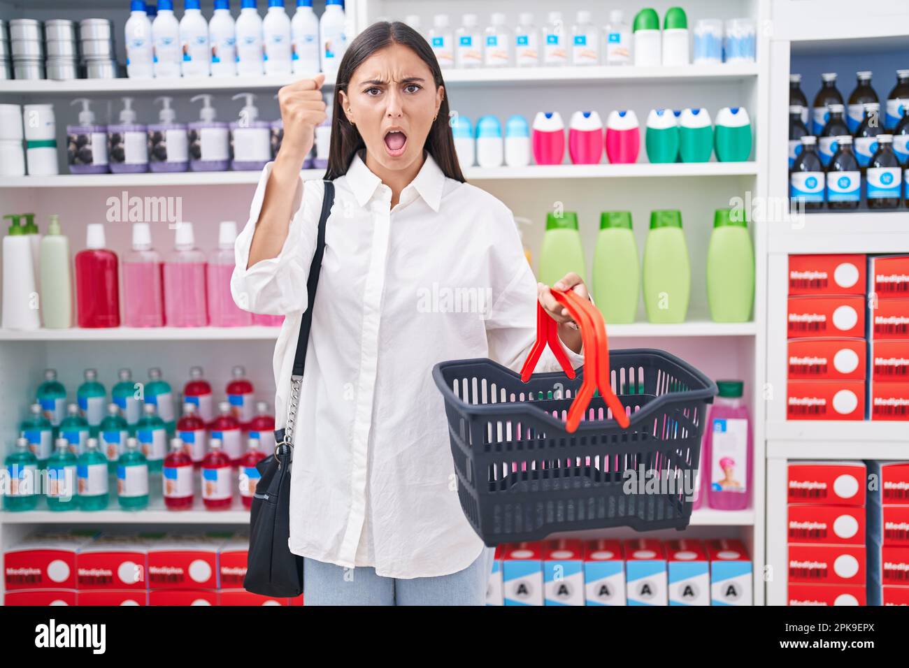 Young hispanic woman shopping at pharmacy drugstore holding basket ...