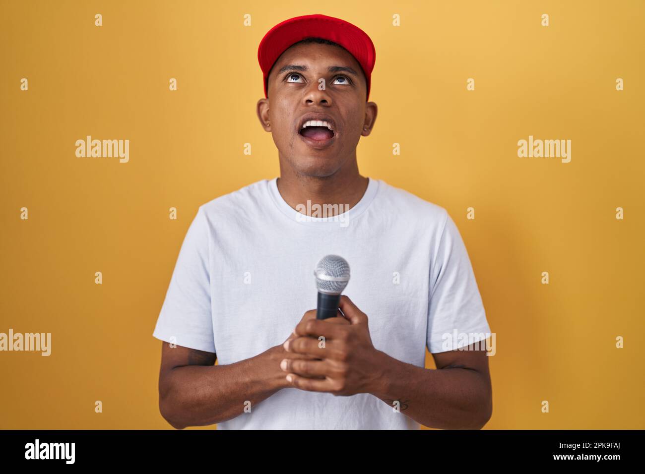 Young hispanic man singing song using microphone angry and mad ...