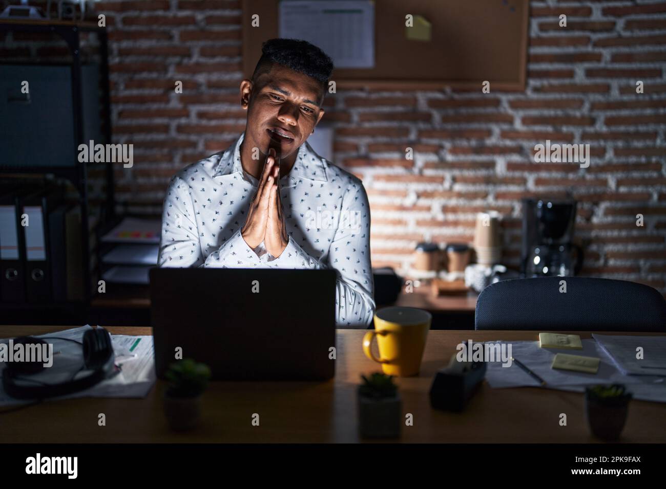 Young hispanic man working at the office at night begging and praying ...