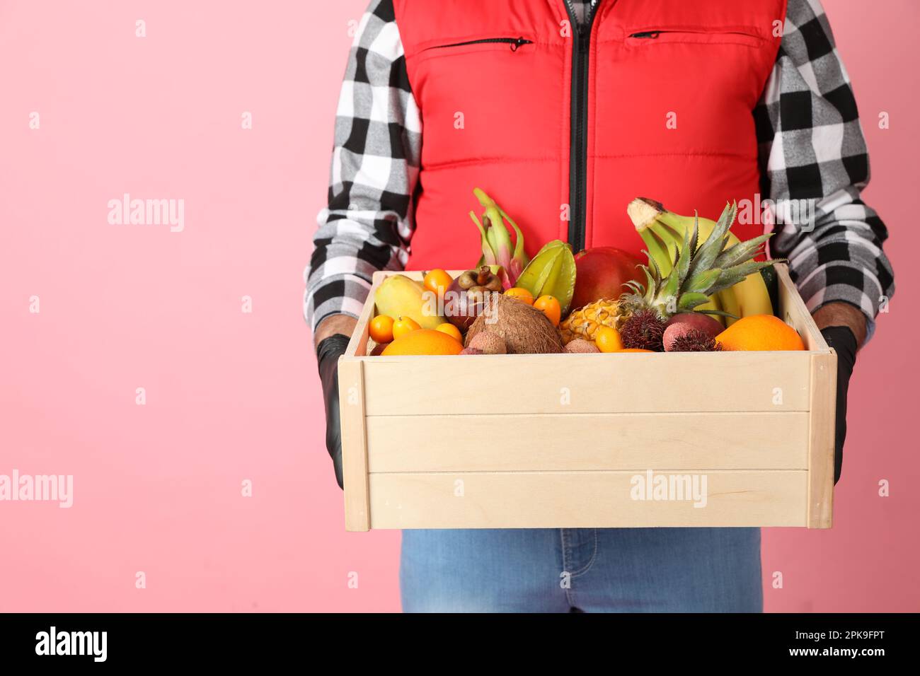 Courier holding crate with assortment of exotic fruits on pink ...