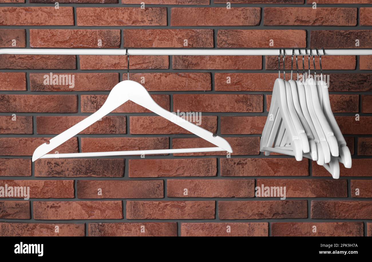 White clothes hangers on rail near red brick wall Stock Photo - Alamy