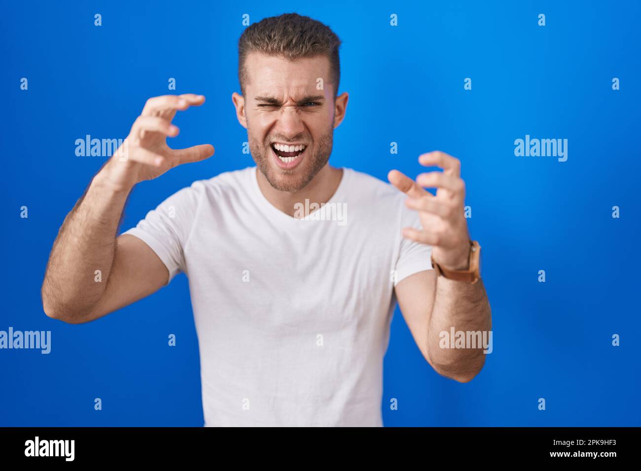 Young caucasian man standing over blue background shouting frustrated ...