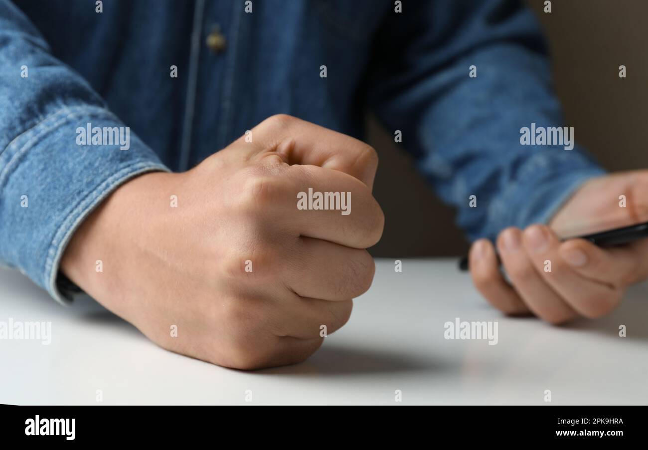 Man with clenched fist holding mobile phone at table, closeup ...