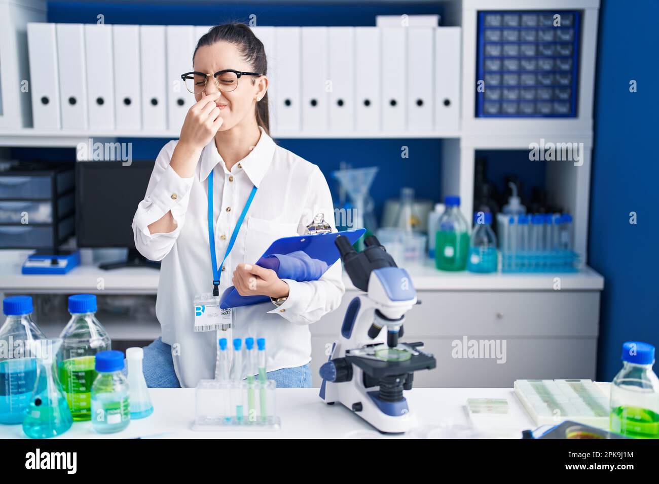 Young brunette woman working at scientist laboratory smelling something ...