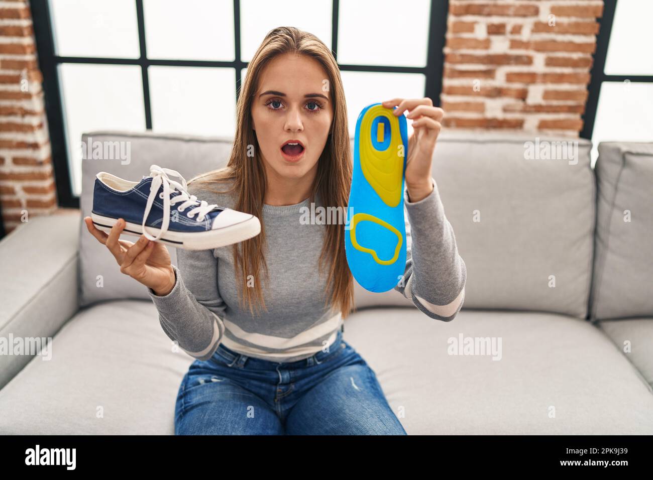 Young woman holding shoe insole in shock face, looking skeptical and ...