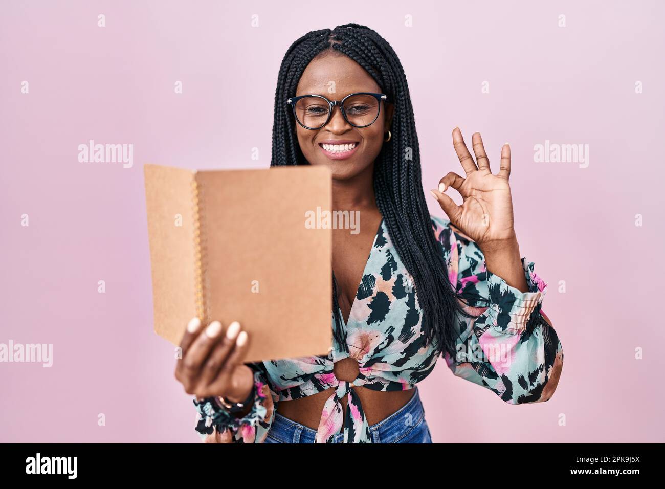 African woman with braids reading a book doing ok sign with fingers ...