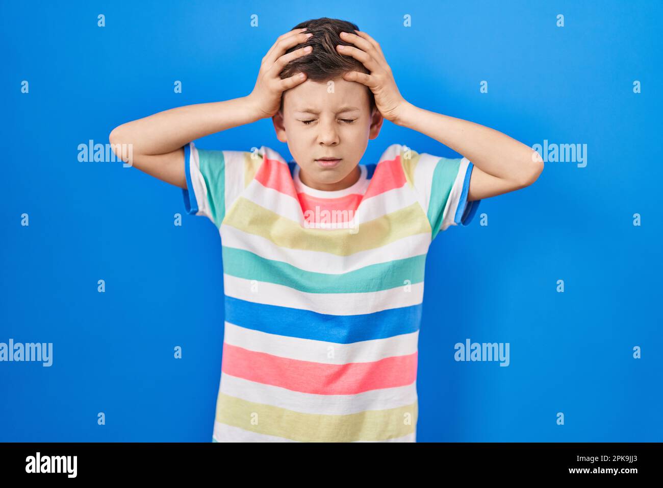 Young caucasian kid standing over blue background suffering from ...