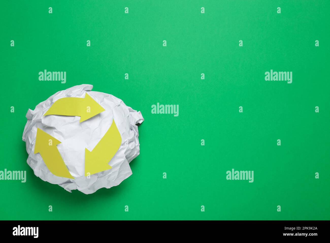 Crumpled paper with recycling symbol on green background, top view ...