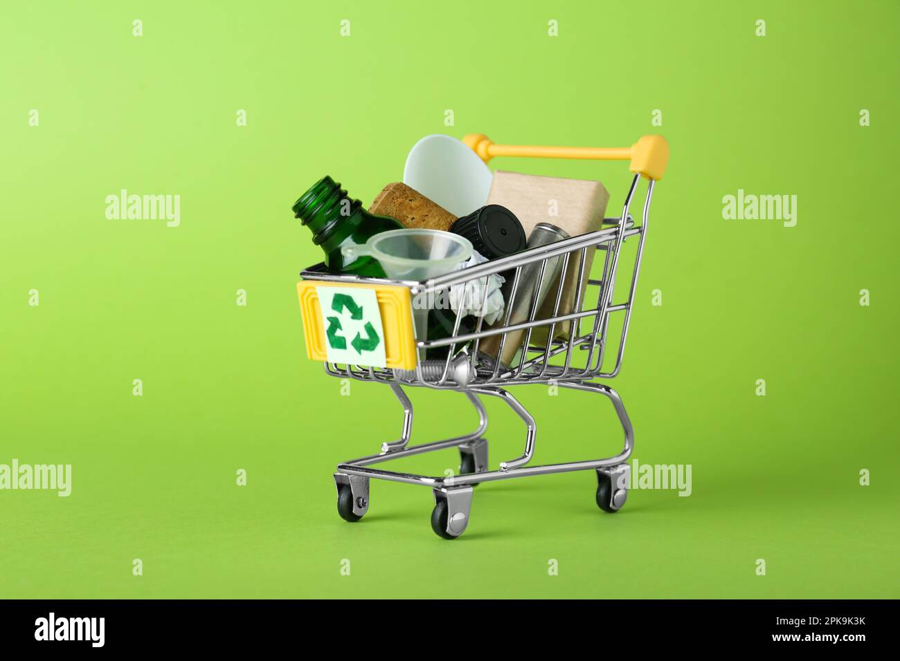 Shopping cart with recycling symbol full of garbage on light green ...