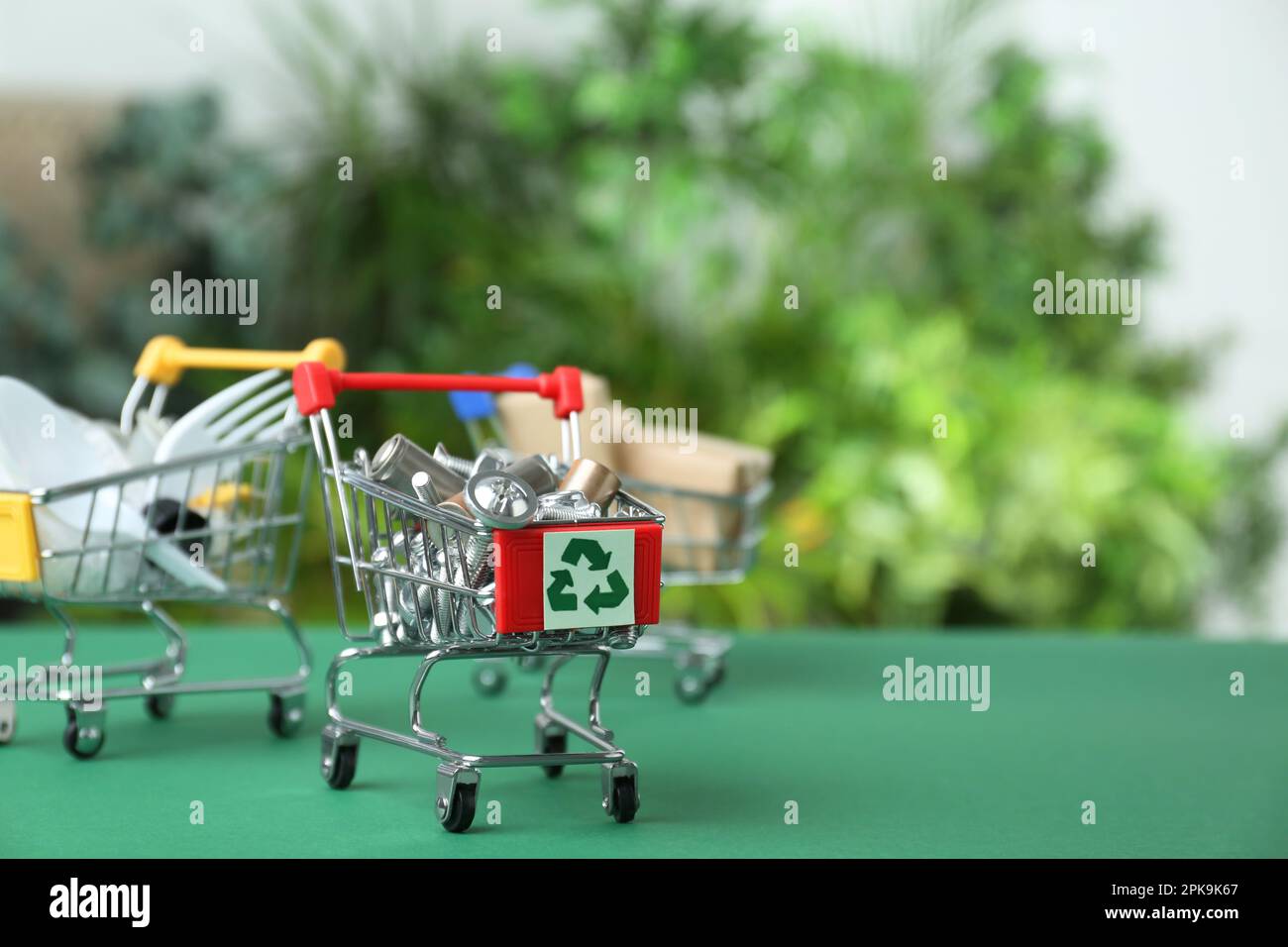 Shopping cart with recycling symbol full of garbage on green table ...