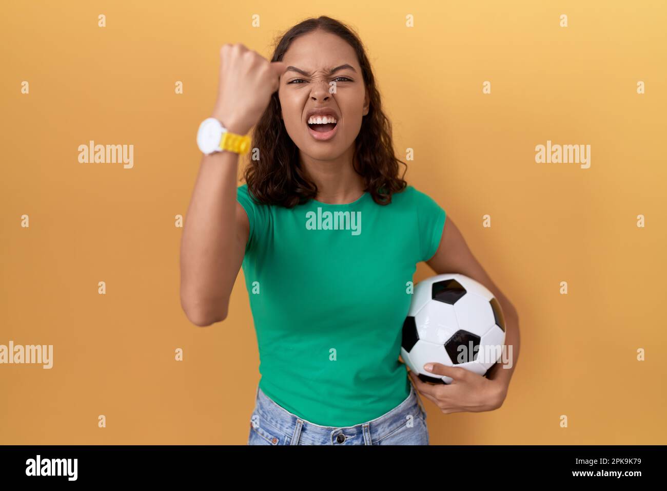 Young hispanic woman holding ball angry and mad raising fist frustrated ...