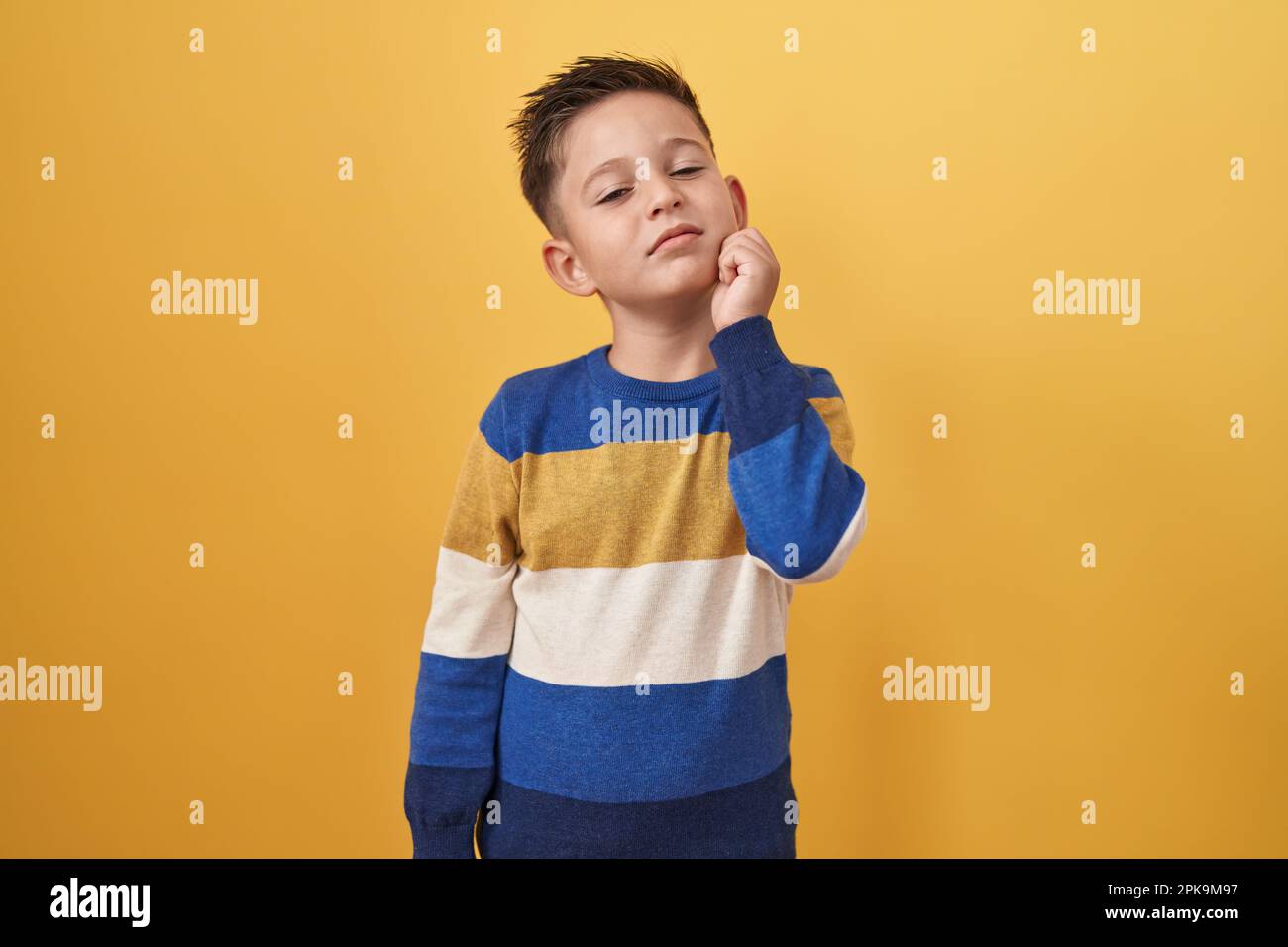 Little hispanic boy standing over yellow background thinking ...