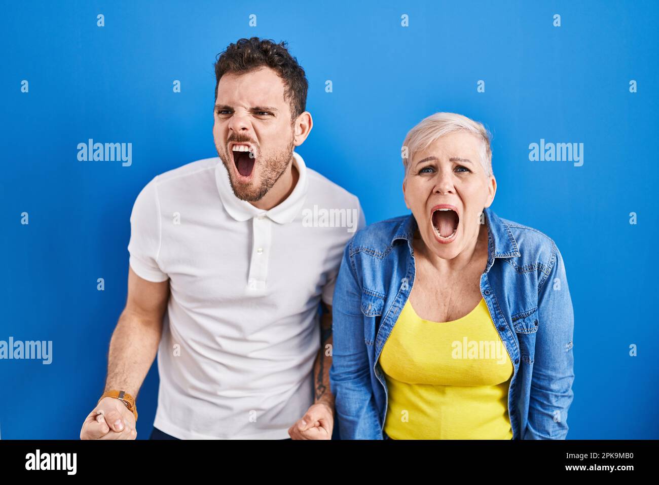 Young brazilian mother and son standing over blue background angry and ...