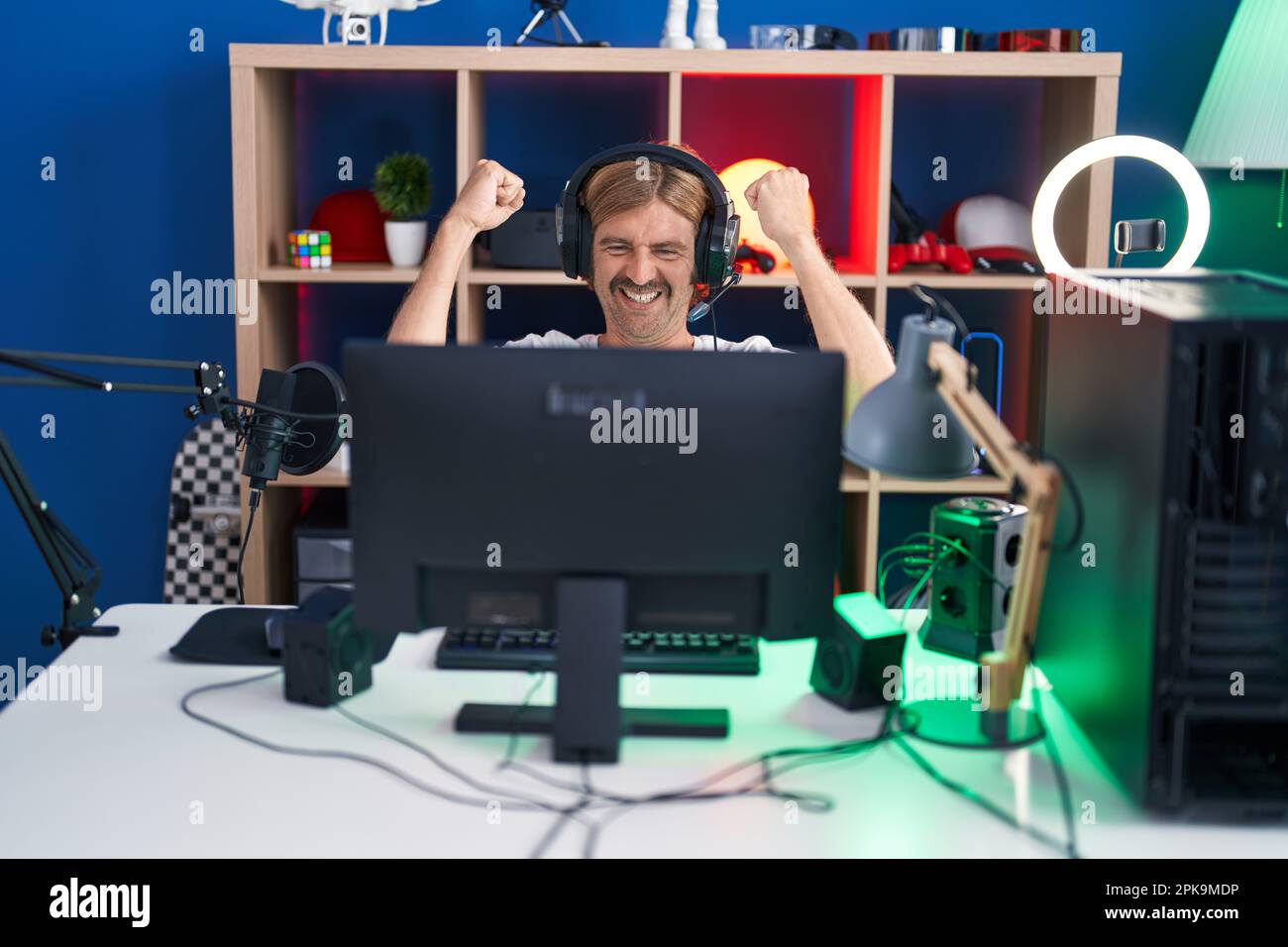 Young blond man streamer playing video game with winner expression at ...