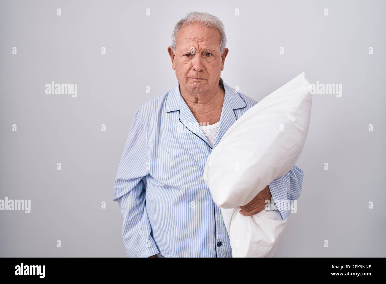 Senior man with grey hair wearing pijama hugging pillow depressed and ...
