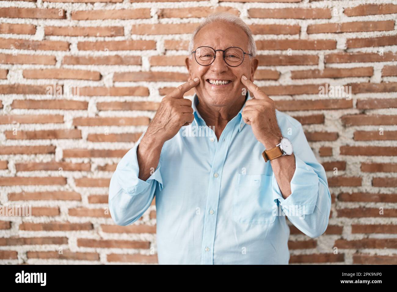 Senior man with grey hair standing over bricks wall smiling with open ...