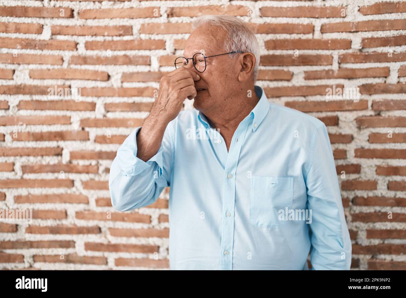 Senior man with grey hair standing over bricks wall smelling something ...
