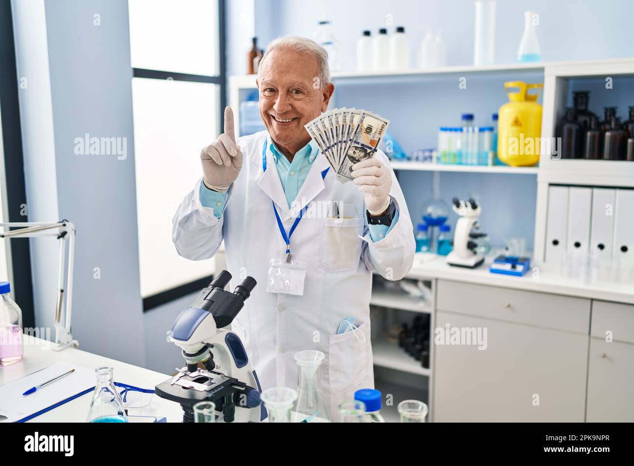Senior scientist with grey hair working at laboratory holding dollars ...