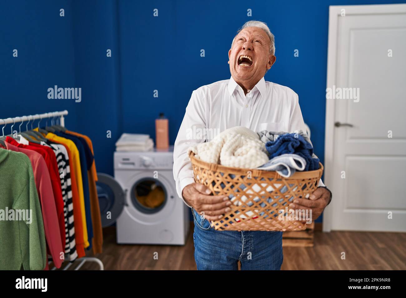 Senior man with grey hair holding laundry basket at home angry and mad ...