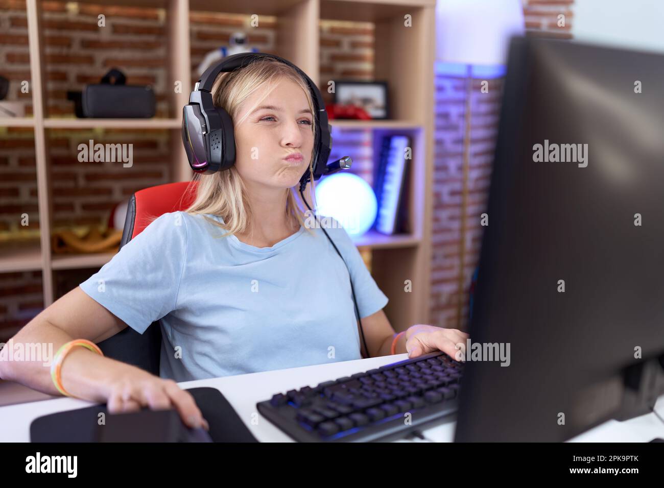 Young caucasian woman playing video games wearing headphones puffing ...