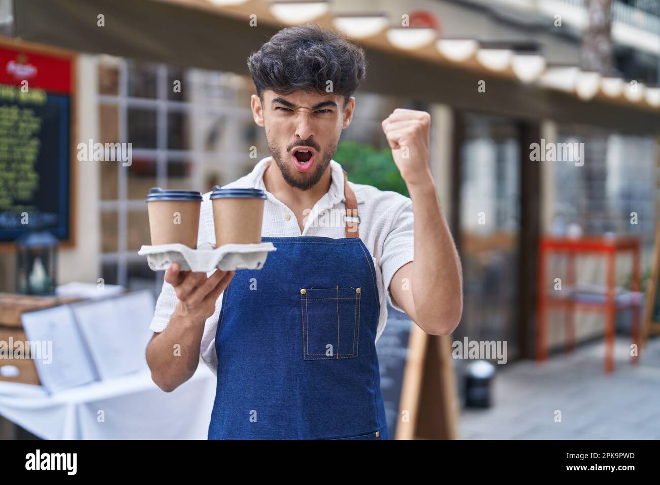 Arab man with beard wearing waiter apron at restaurant terrace annoyed ...