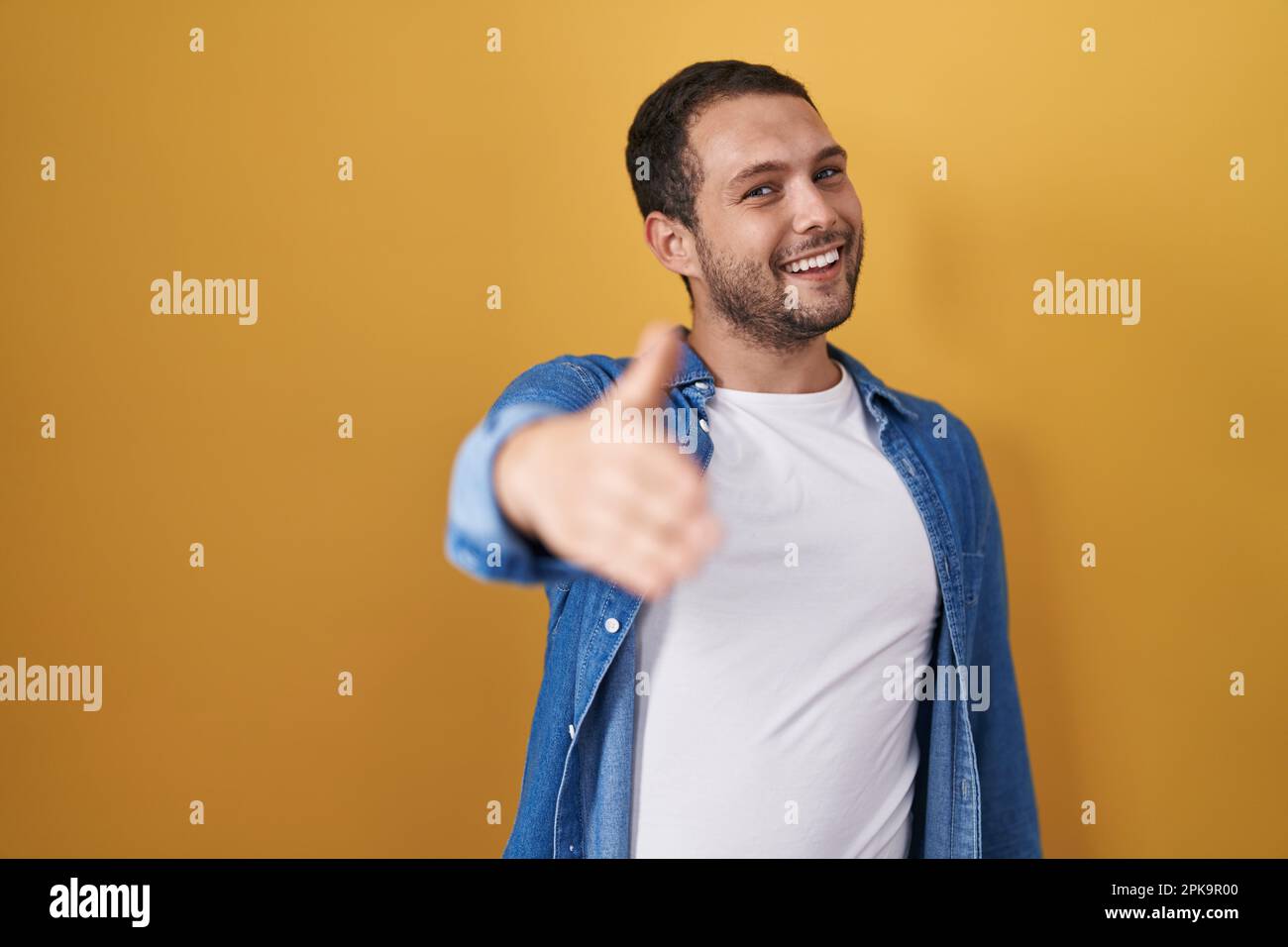 Hispanic man standing over yellow background smiling friendly offering ...