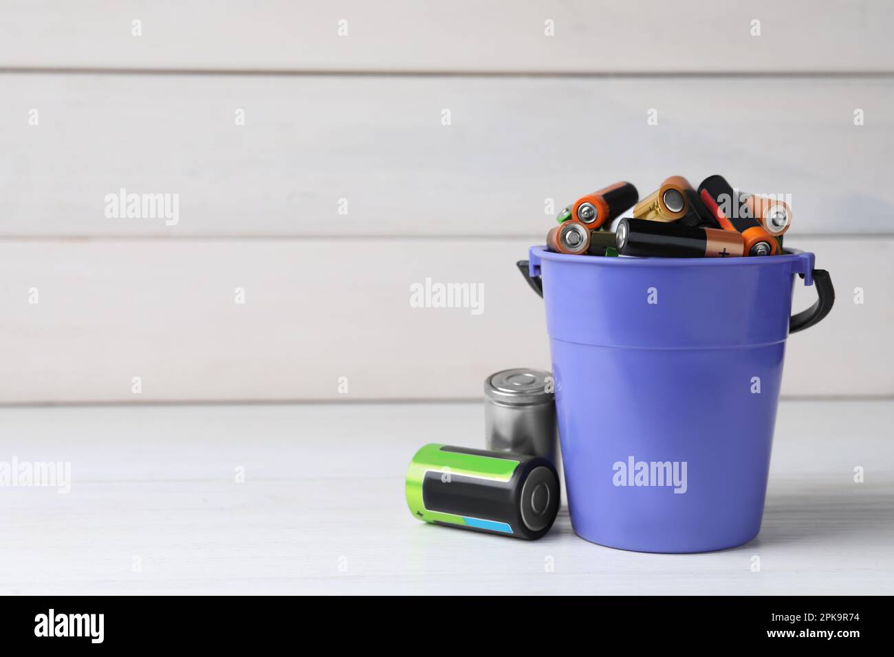Many different used electric batteries in bucket on white wooden table ...