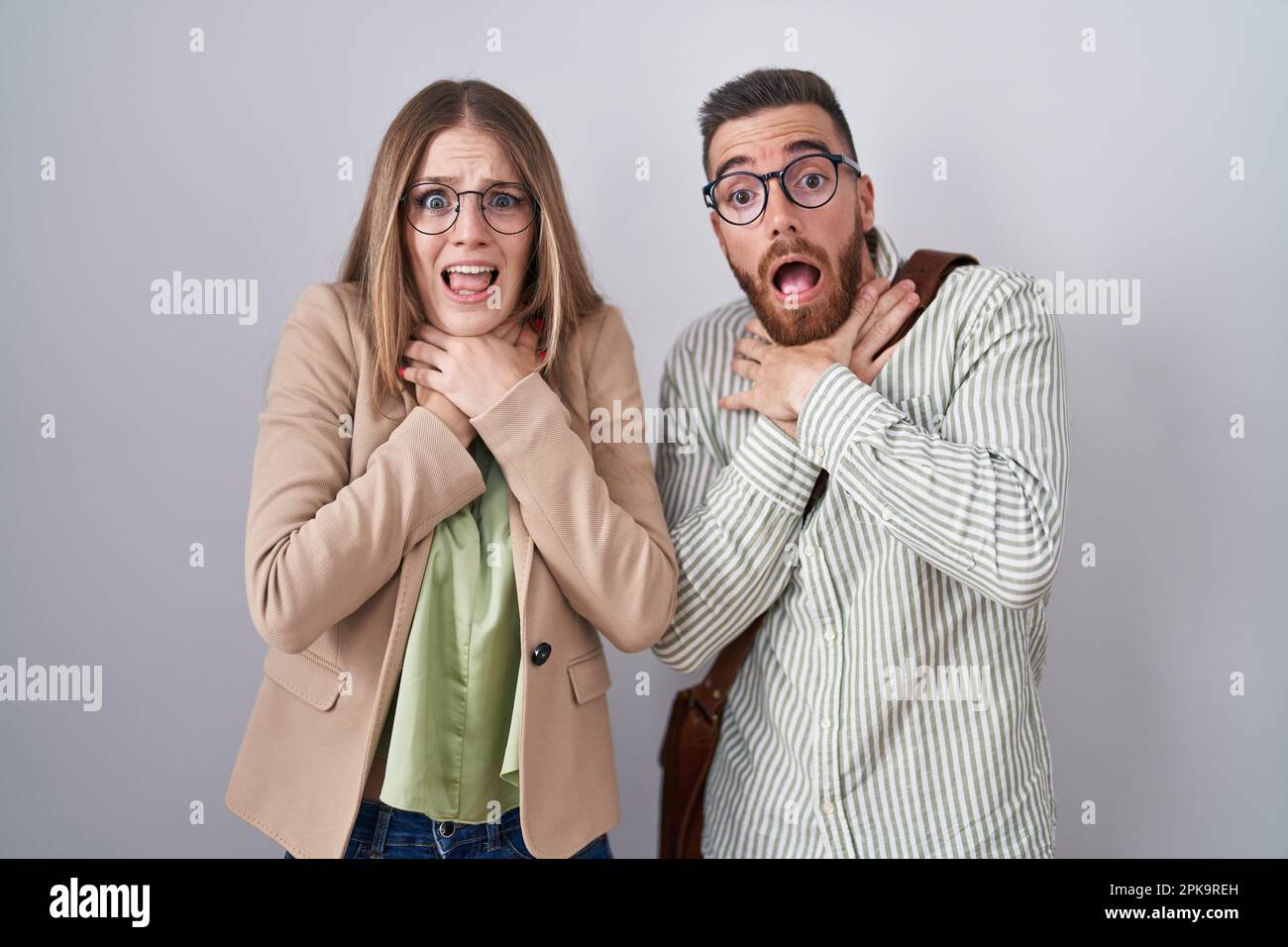 Young couple standing over white background shouting and suffocate ...