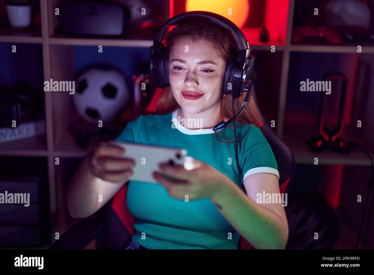 Young redhead woman streamer playing video game using smartphone at ...
