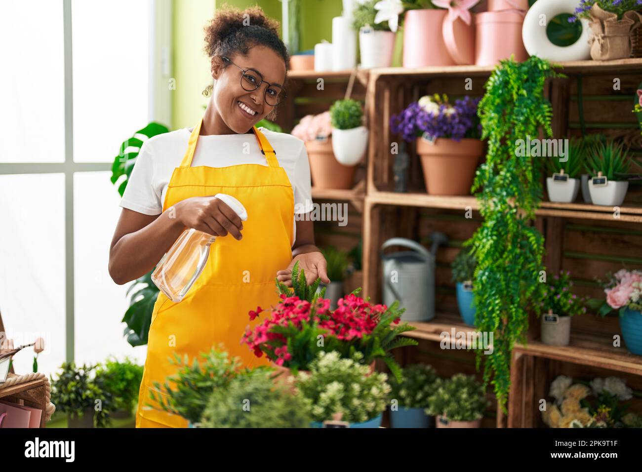African american woman florist using diffuser watering plant at flower ...
