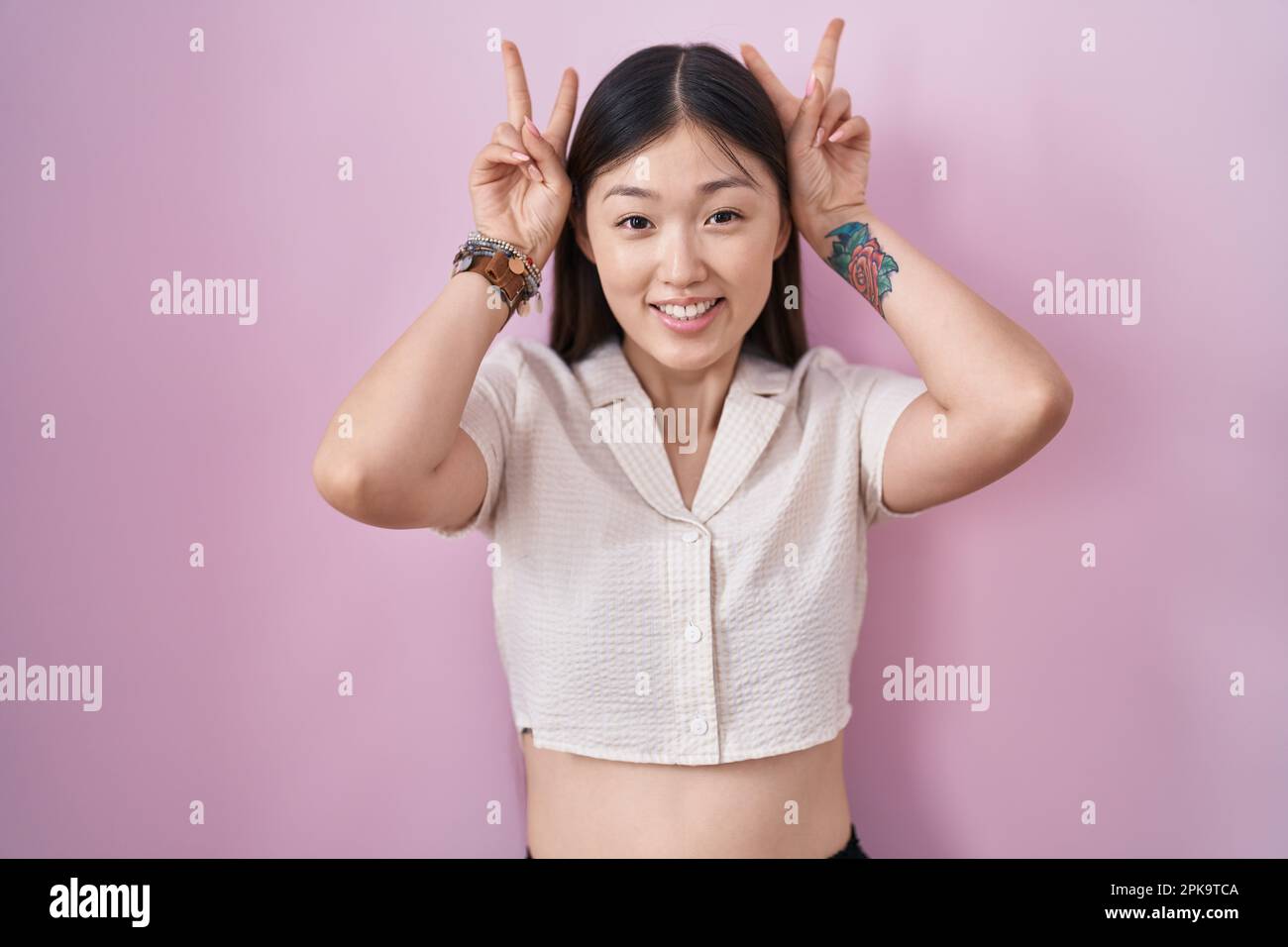 Chinese young woman standing over pink background posing funny and ...