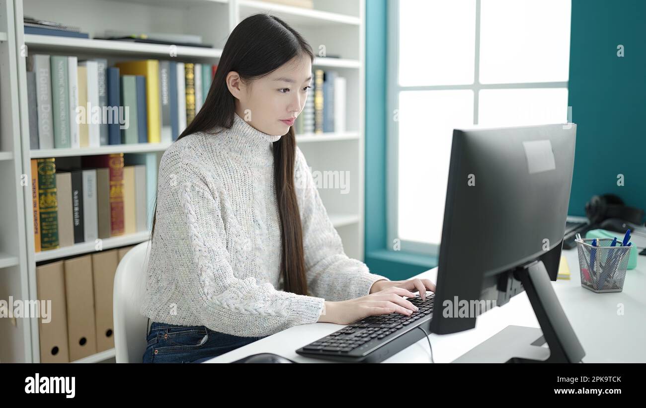 Young chinese woman student using computer studying at library ...
