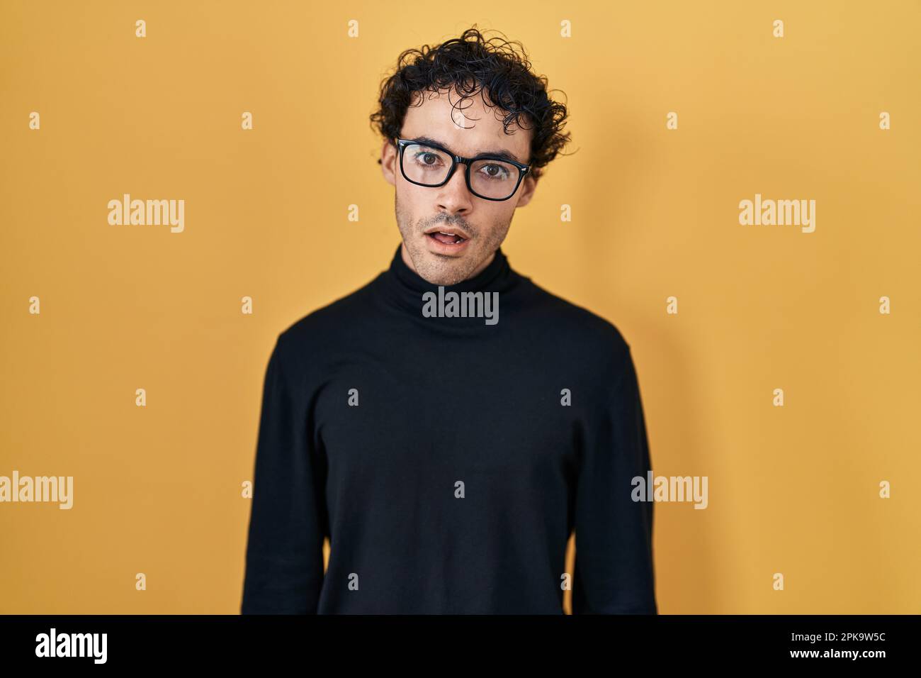 Hispanic man standing over yellow background in shock face, looking ...