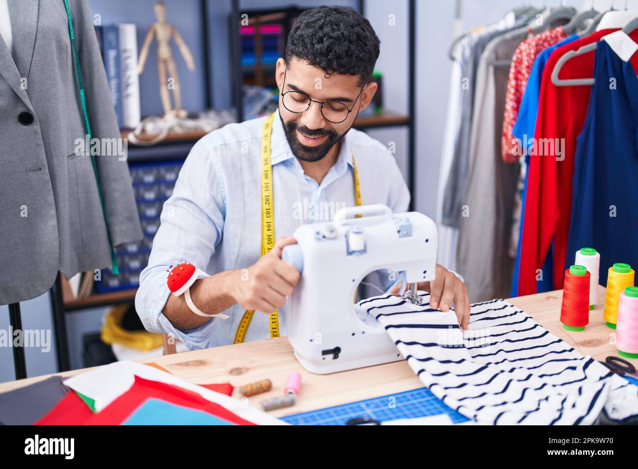 Young arab man tailor smiling confident using sewing machine at tailor ...