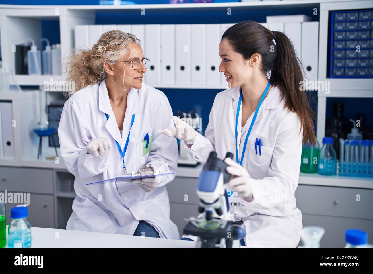 Two women scientists using microscope write on document at laboratory ...
