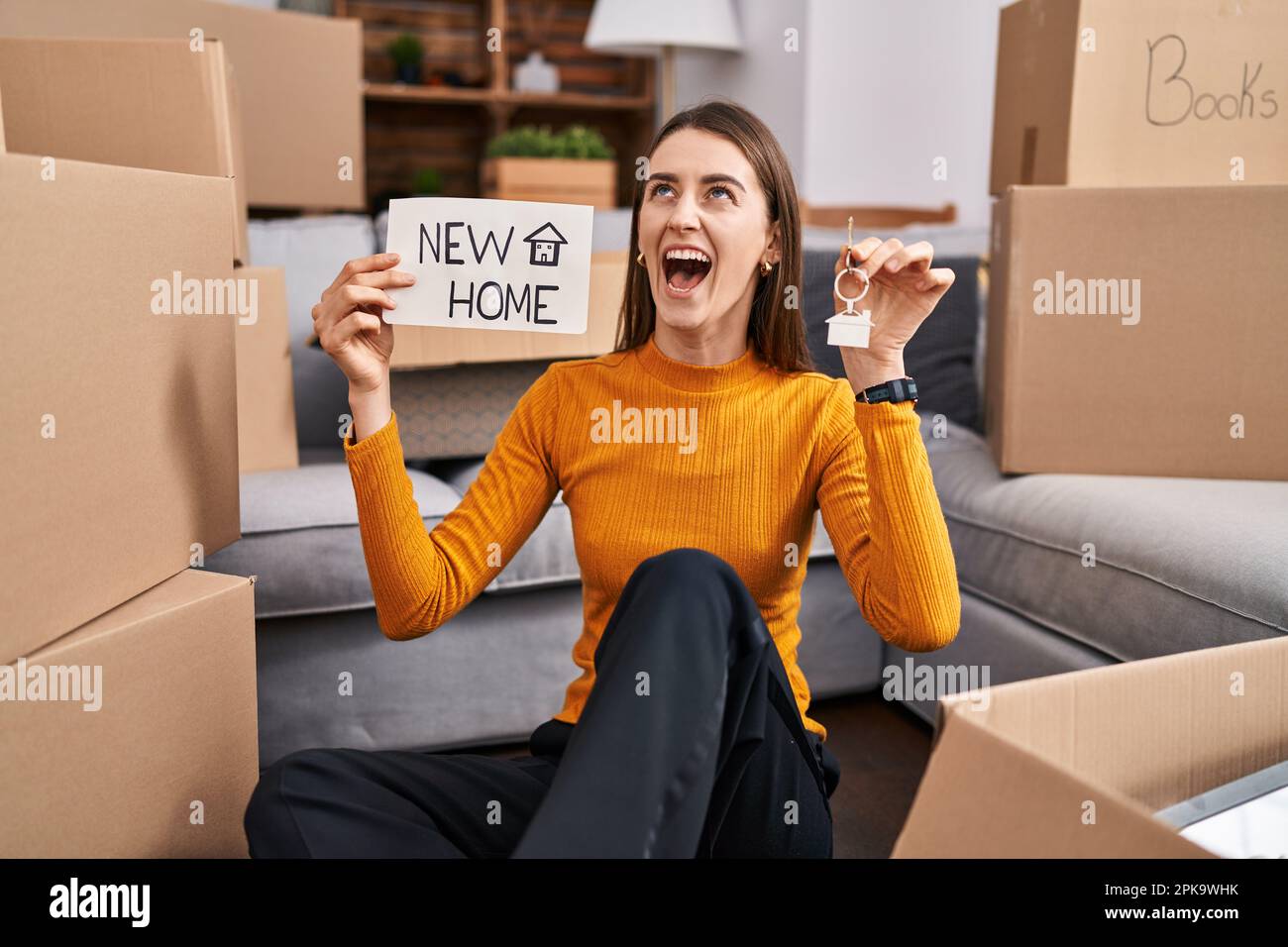 Young caucasian woman sitting on the floor at new home holding new home ...