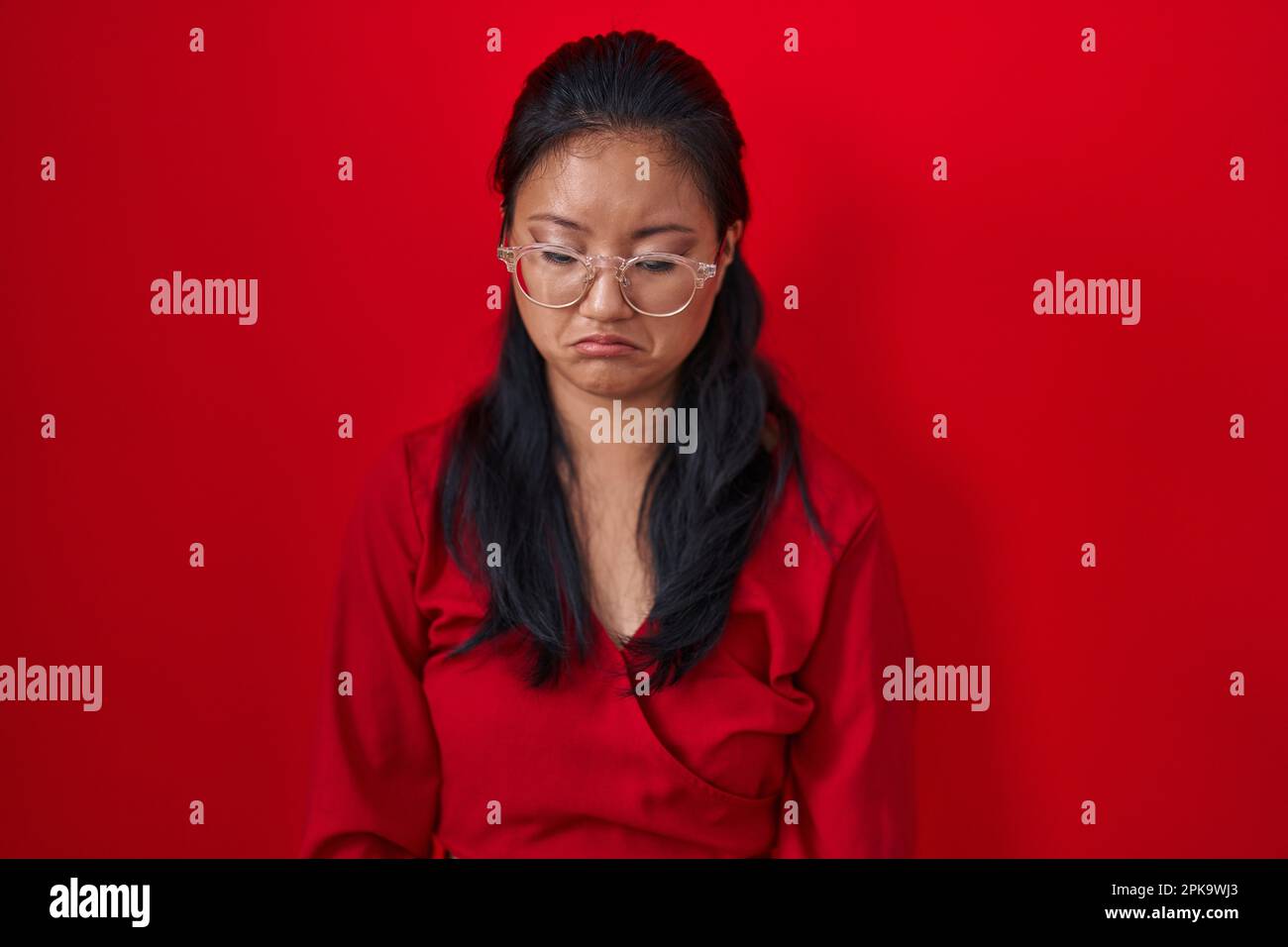 Asian young woman standing over red background depressed and worry for ...