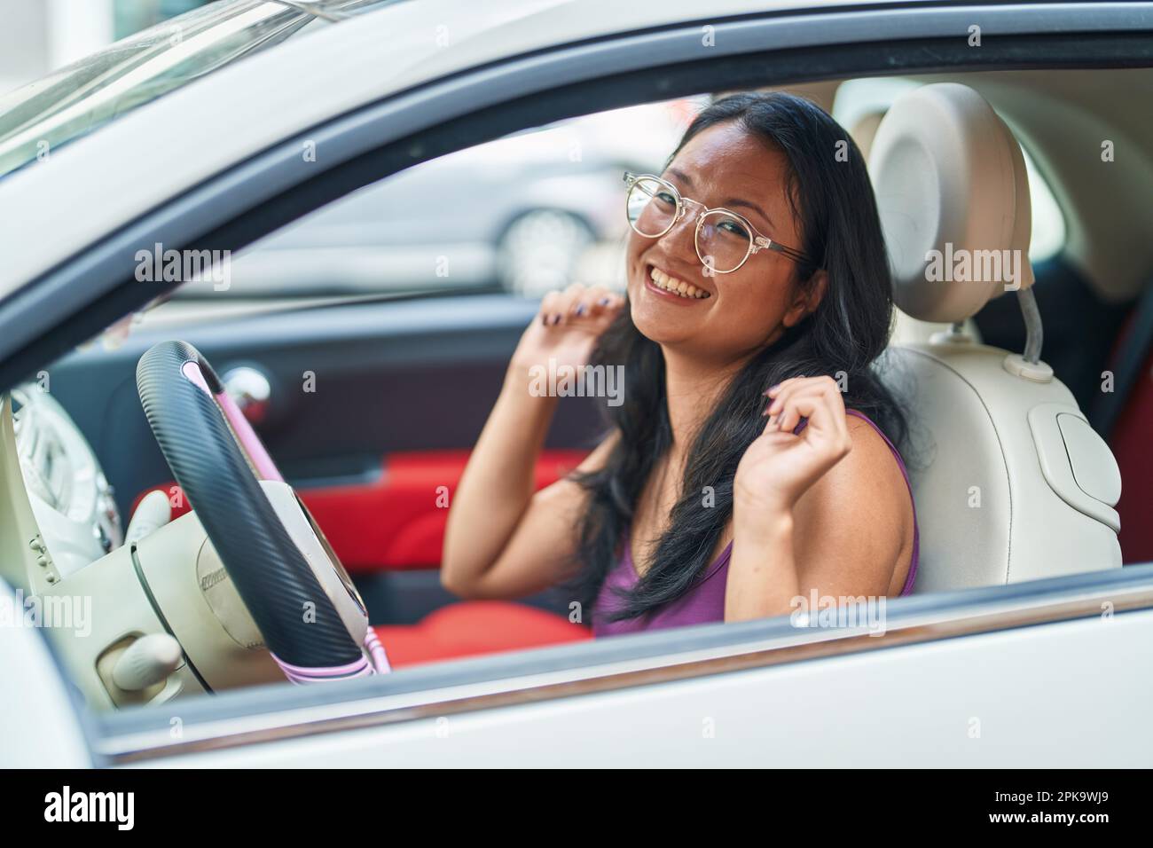 Young chinese woman sitting on car dancing at street Stock Photo - Alamy