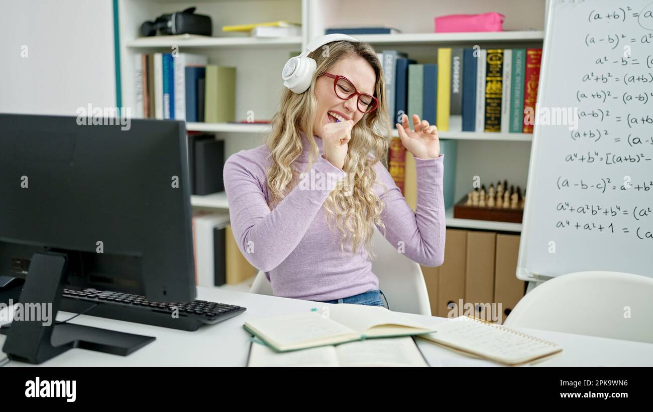 Young blonde woman student listening to music singing song at classroom ...