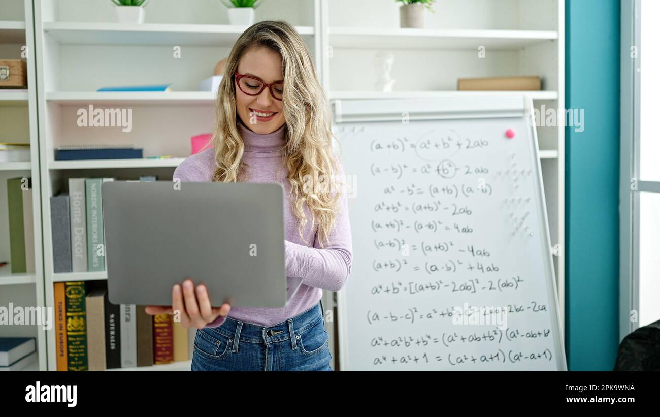 Young blonde woman teacher teaching maths lesson holding laptop at ...