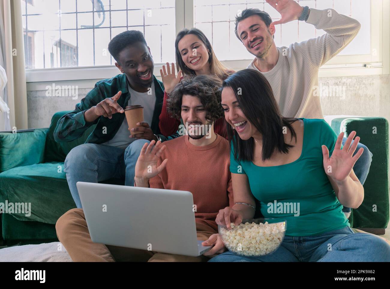 Five multi-ethnic millennial friends sitting on sofa looking at ...