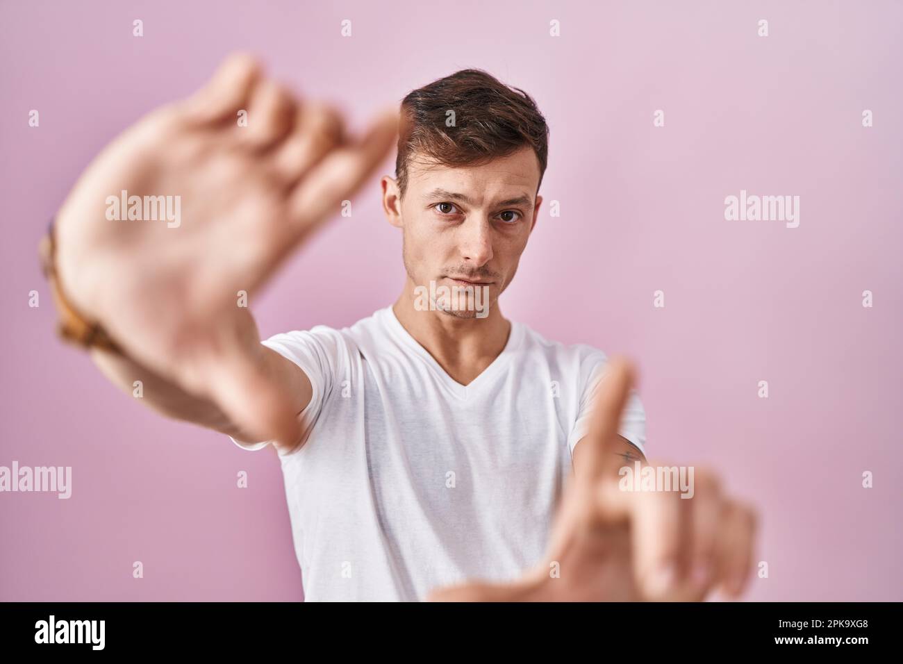 Caucasian man standing over pink background doing frame using hands ...