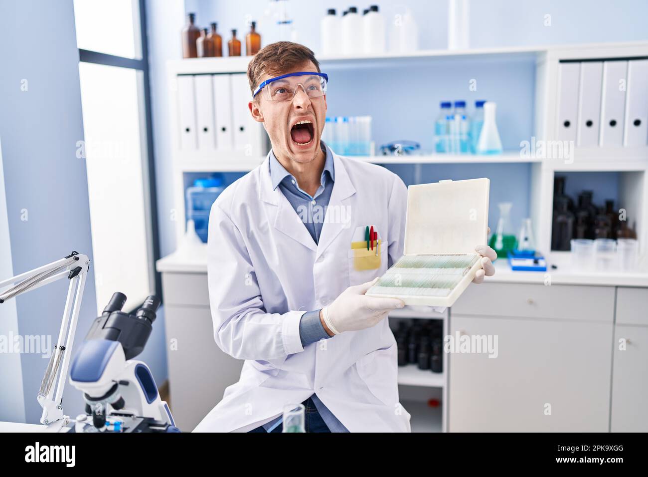 Caucasian man working at scientist laboratory angry and mad screaming ...