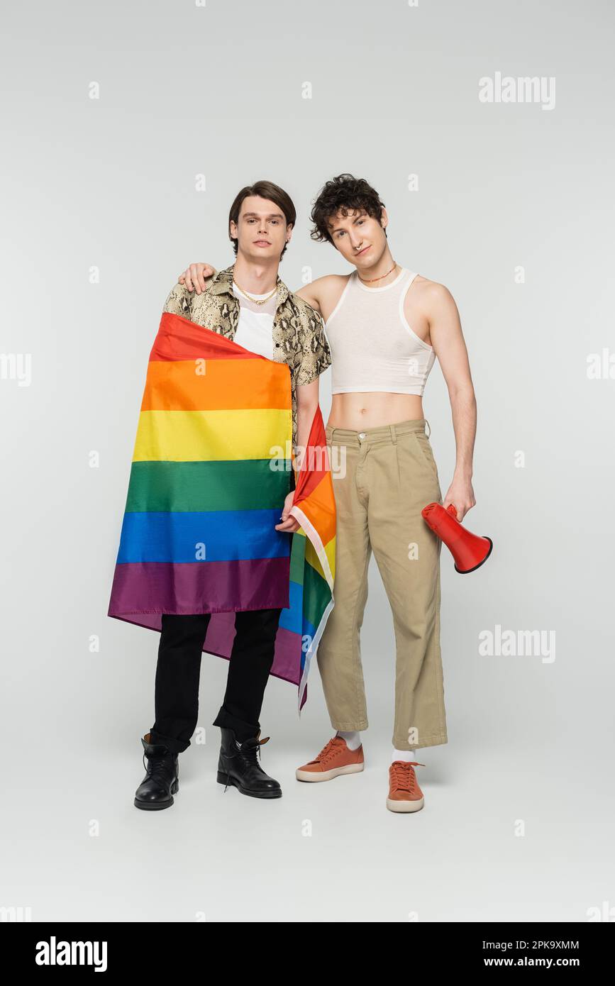 full length of young nonbinary couple with lgbt flag and megaphone ...