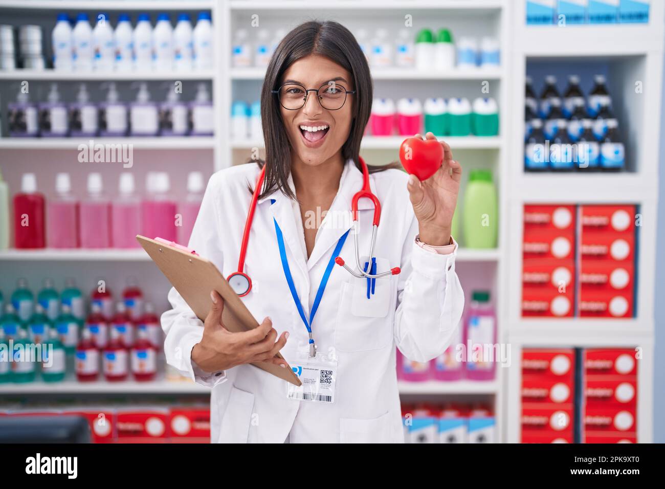 Brunette young woman working at pharmacy drugstore holding red heart ...