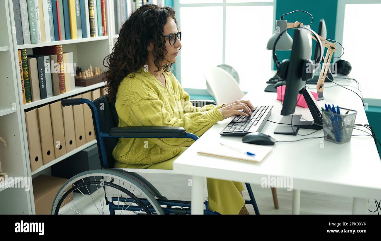 Middle age hispanic woman teacher using computer sitting on wheelchair ...