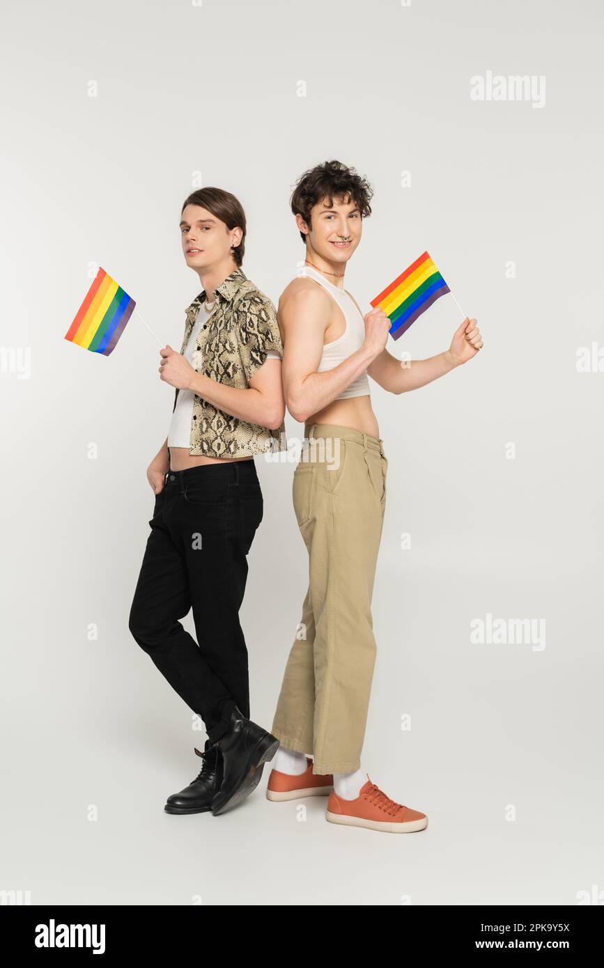 full length of stylish pansexual models posing with small lgbt flags on ...