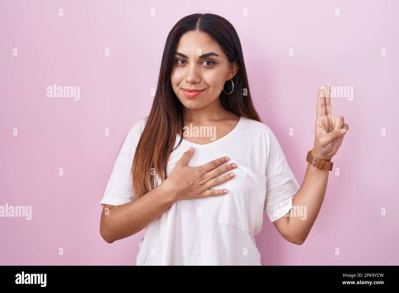 Young arab woman standing over pink background smiling swearing with ...