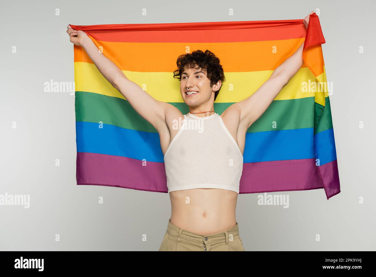 joyful bigender model in crop top holding lgbt flag in raised hands and ...